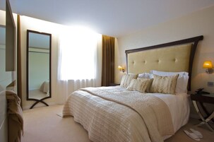 Quarto de hotel com uma cama grande, um espelho, uma mesa de cabeceira com abajur e vista para o exterior.