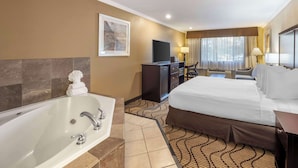 Quarto de hotel com uma cama grande, uma escrivaninha com cadeira, televisão de tela plana, abajur e banheira.