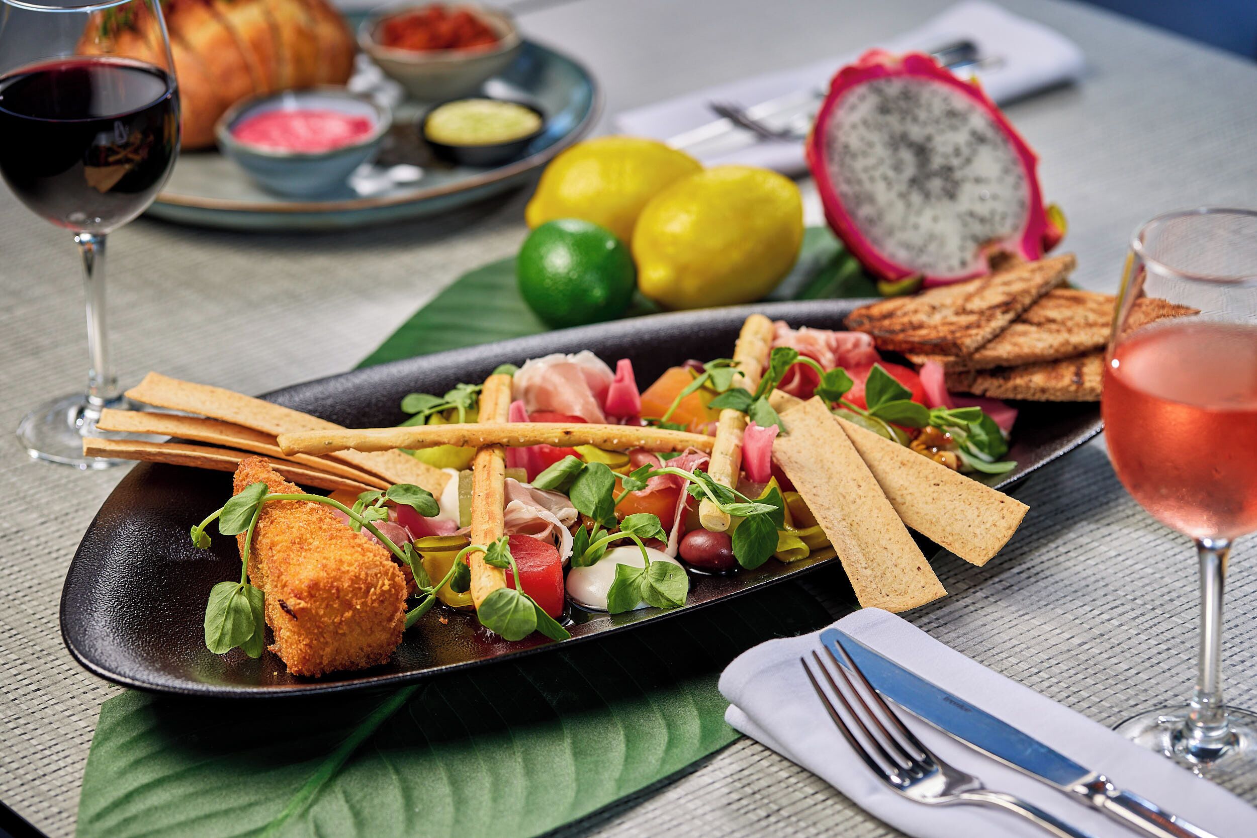 Um prato de comida com salada, pão e um copo de vinho sobre uma mesa.