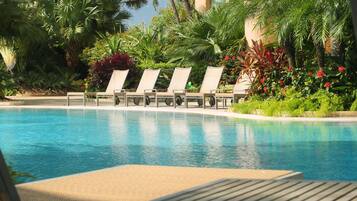 Piscina com espreguiçadeiras e plantas tropicais.