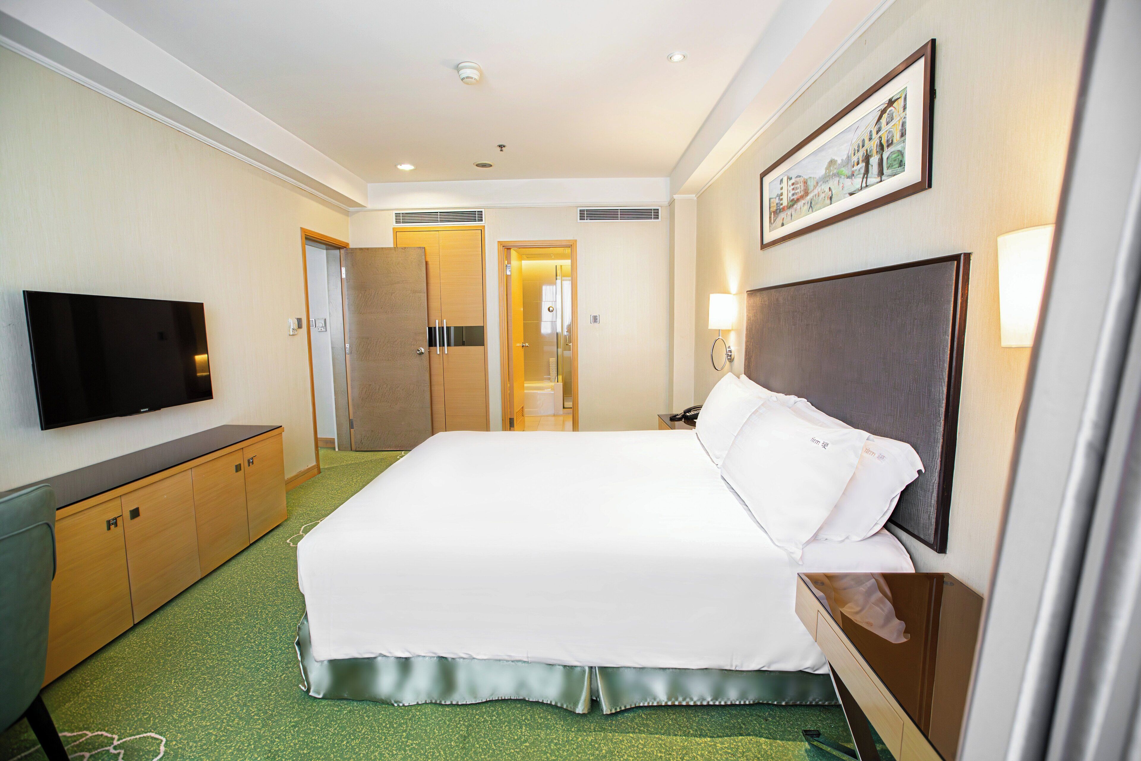 Quarto de hotel com uma cama grande, televisão, escrivaninha e guarda-roupa.