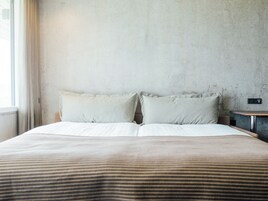 Cama com duas almofadas, cabeceira de madeira e mesa de cabeceira com abajur.