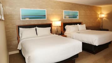 Quarto de hotel com duas camas, cabeceira de madeira, mesa de cabeceira com abajur e dois quadros na parede.