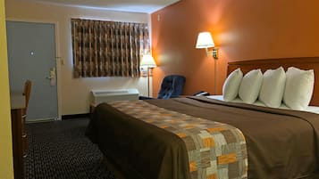 Quarto de hotel com cama, uma cadeira, escrivaninha, luminária e ar condicionado fixado na parede.