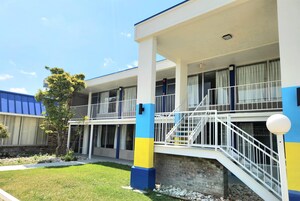 Um motel de dois andares com uma varanda no andar superior, uma escadaria que leva ao nível superior e uma pequena árvore no quintal da frente.