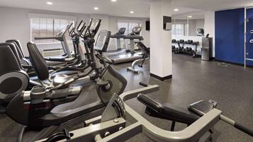 Uma academia com diversos equipamentos de cardio, bancos de peso e halteres.