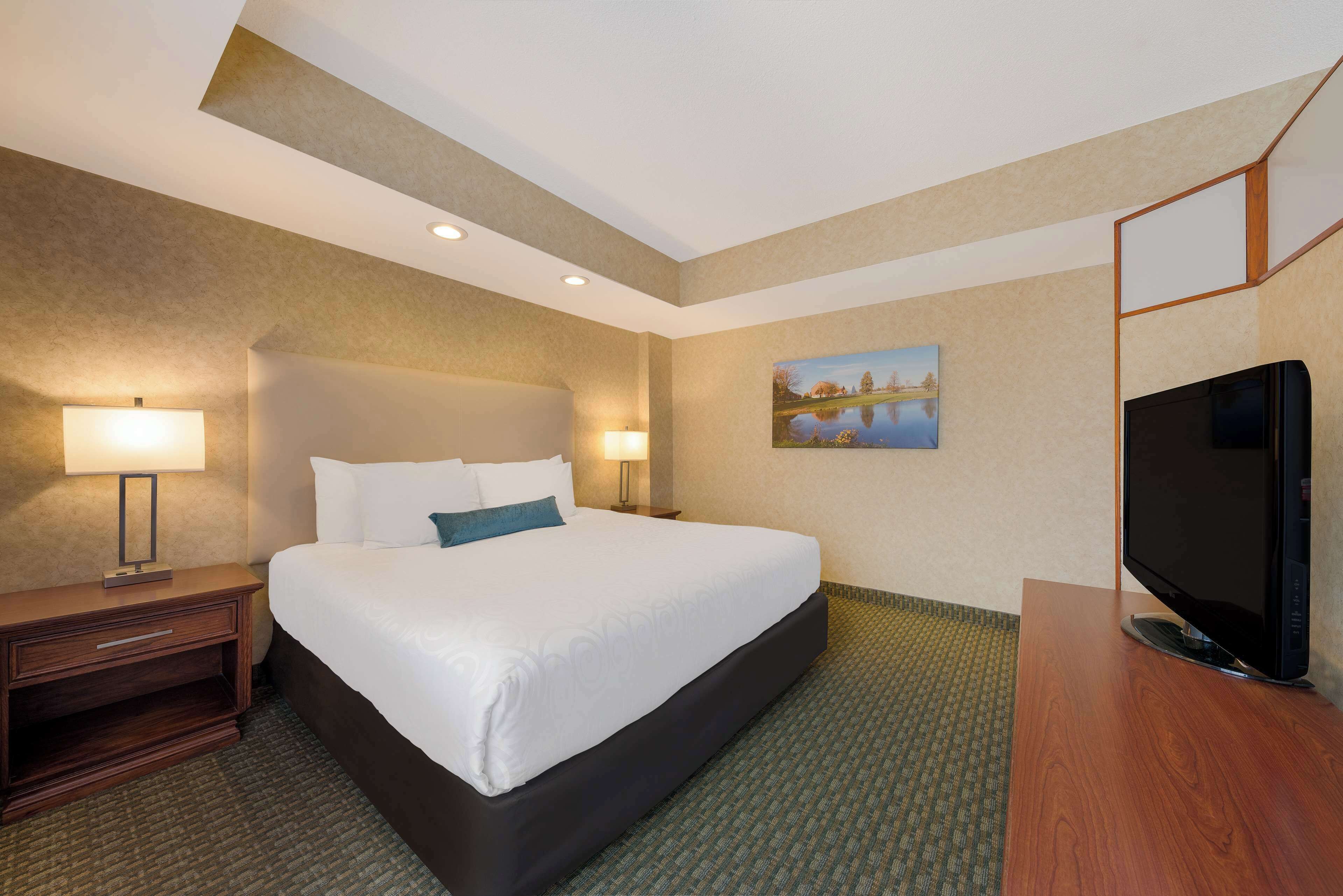 Quarto de hotel com uma cama grande, duas luminárias de cabeceira, uma televisão de tela plana e um quadro na parede.