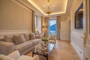 Quarto de hotel com sofá, mesa de centro com um livro, abajur e vista para o mar.