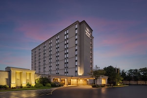 Um hotel com vários andares, um letreiro chamativo, estacionamento e uma área de entrada com paisagismo.