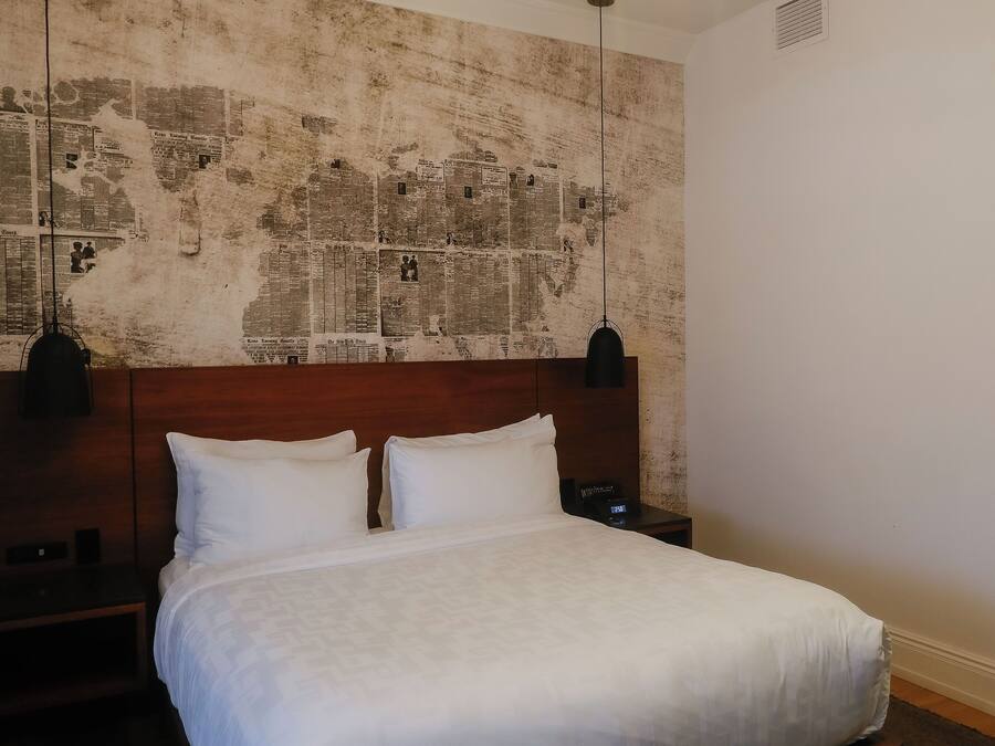 Quarto com uma cama grande, cabeceira de madeira, duas mesas de cabeceira e uma parede com mural de jornal.