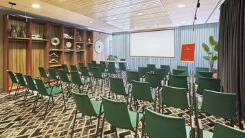Uma sala de conferências com cadeiras verdes, uma tela de projetor e um carpete estampado.