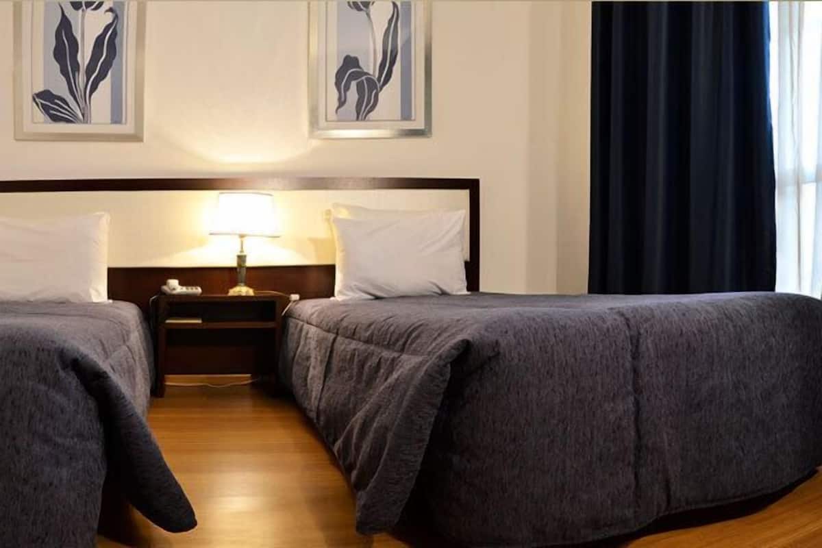 Quarto de hotel com duas camas de solteiro, uma mesa de cabeceira com abajur e obras de arte nas paredes.