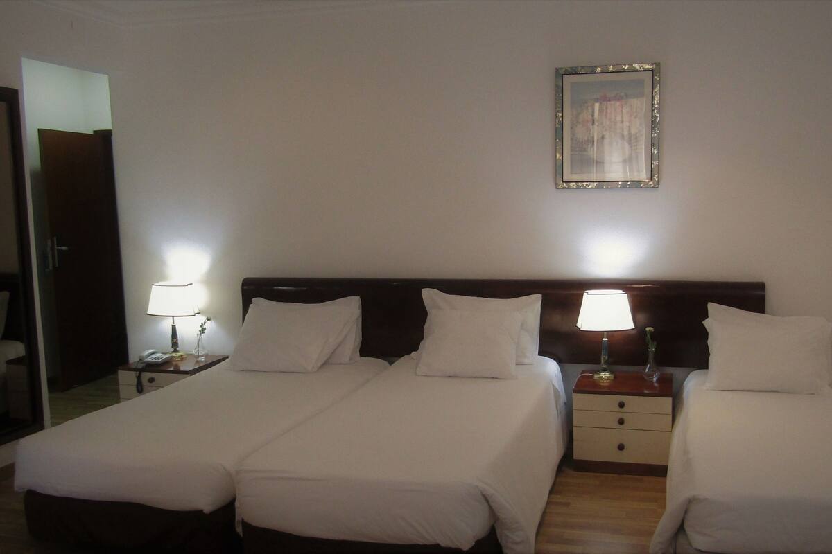 Quarto de hotel com duas camas de solteiro, mesa de cabeceira com luminárias, espelho e um quadro na parede.