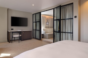 Quarto de hotel com cama, escrivaninha e cadeira, televisão e porta de correr para o banheiro.