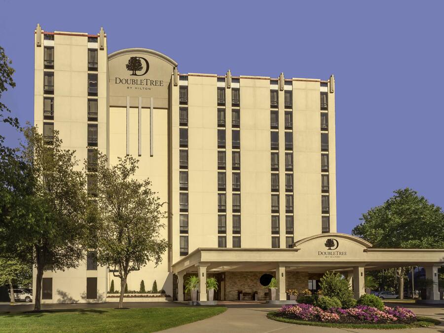 Um hotel com um grande letreiro 'DOUBLETREE', entrada central coberta e fachada simétrica com várias janelas.