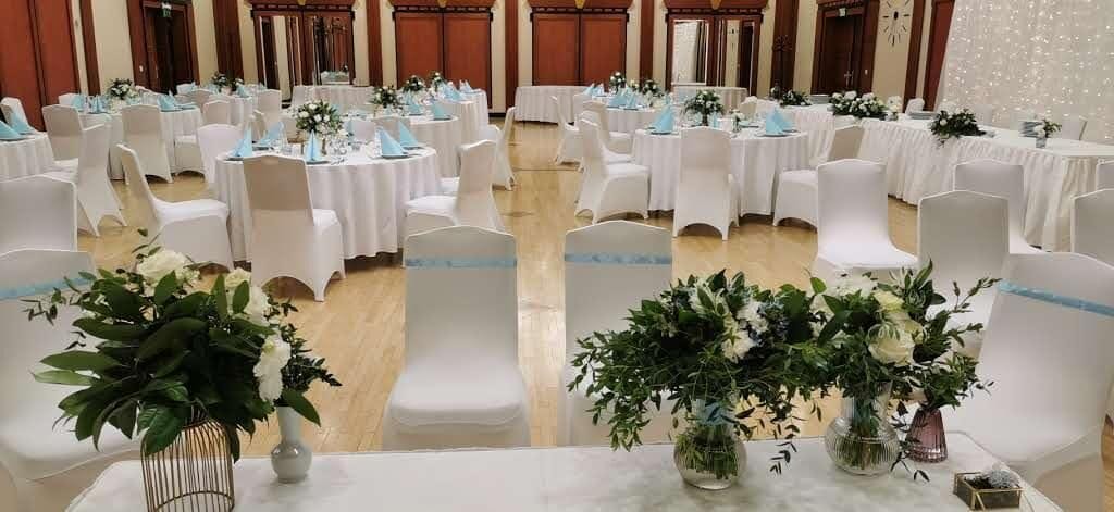 Uma sala de banquetes com mesas redondas, cadeiras brancas e centros de mesa florais.