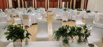 Uma sala de banquetes com mesas redondas, cadeiras brancas e centros de mesa florais.