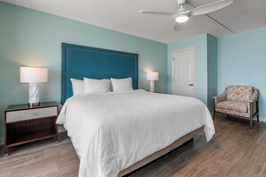 Um quarto com cama, mesas de cabeceira, uma cadeira e uma porta.