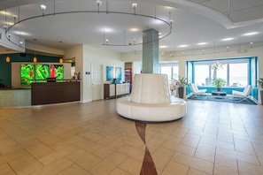 Um hall espaçoso com uma coluna branca central, balcão de recepção e área de estar com vista.