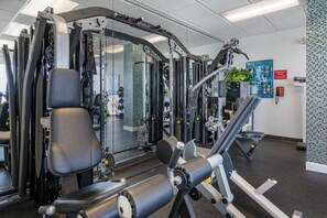Uma academia com diversos equipamentos de exercício, um espelho e uma parede com um pôster.