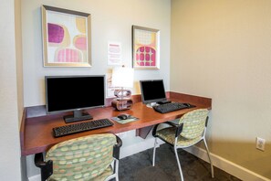 Um espaço de trabalho com dois monitores, um teclado e um rato sobre uma escrivaninha de madeira. Há duas cadeiras com estofados estampados.