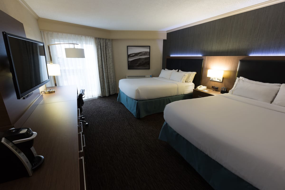 Quarto de hotel com duas camas, televisão, escrivaninha com telefone e janela com cortinas.