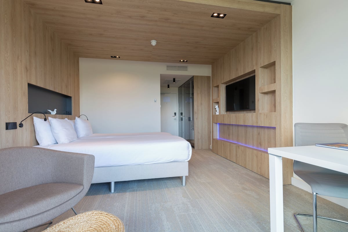 Quarto de hotel moderno com cama, escrivaninha, cadeira e televisão.
