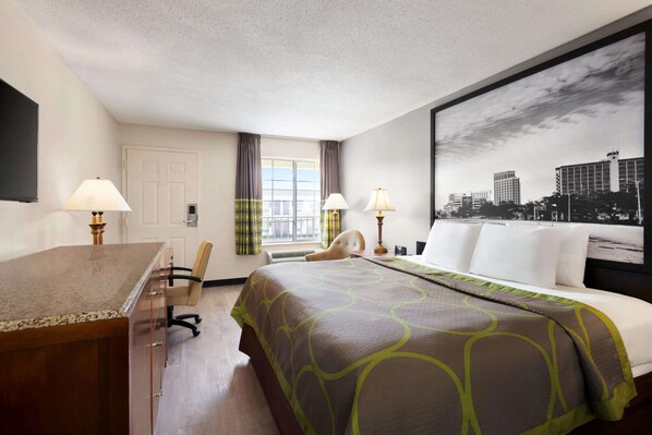 Quarto de hotel com cama, escrivaninha, cadeira e uma pintura com vista para a cidade.