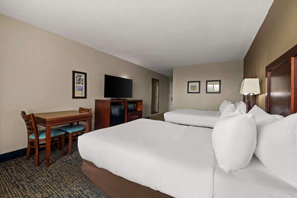 Quarto de hotel com uma cama, uma escrivaninha com cadeira, uma televisão e um abajur.