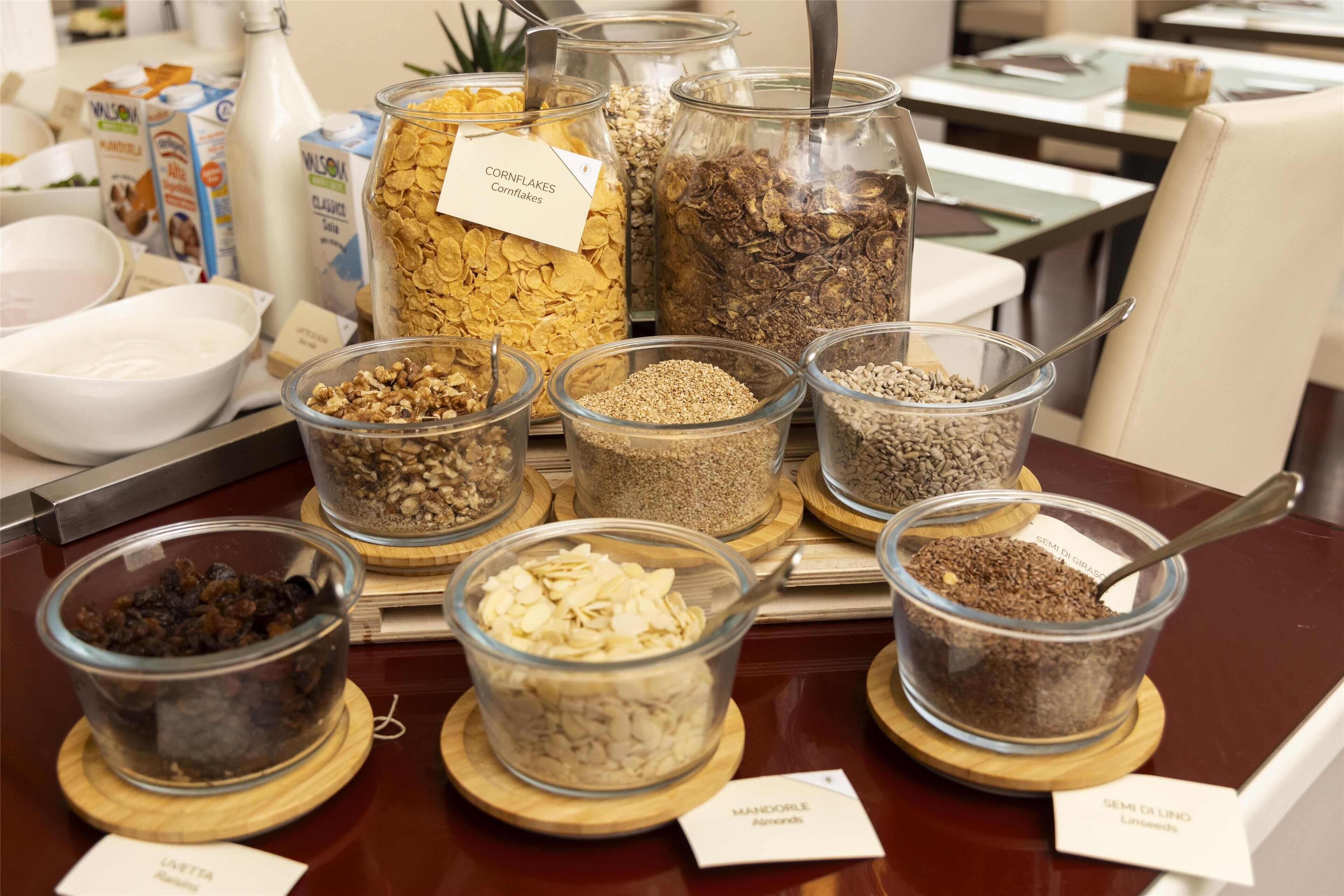 Diversos alimentos expostos em recipientes de vidro sobre uma mesa de madeira, incluindo cereais, nozes e sementes.