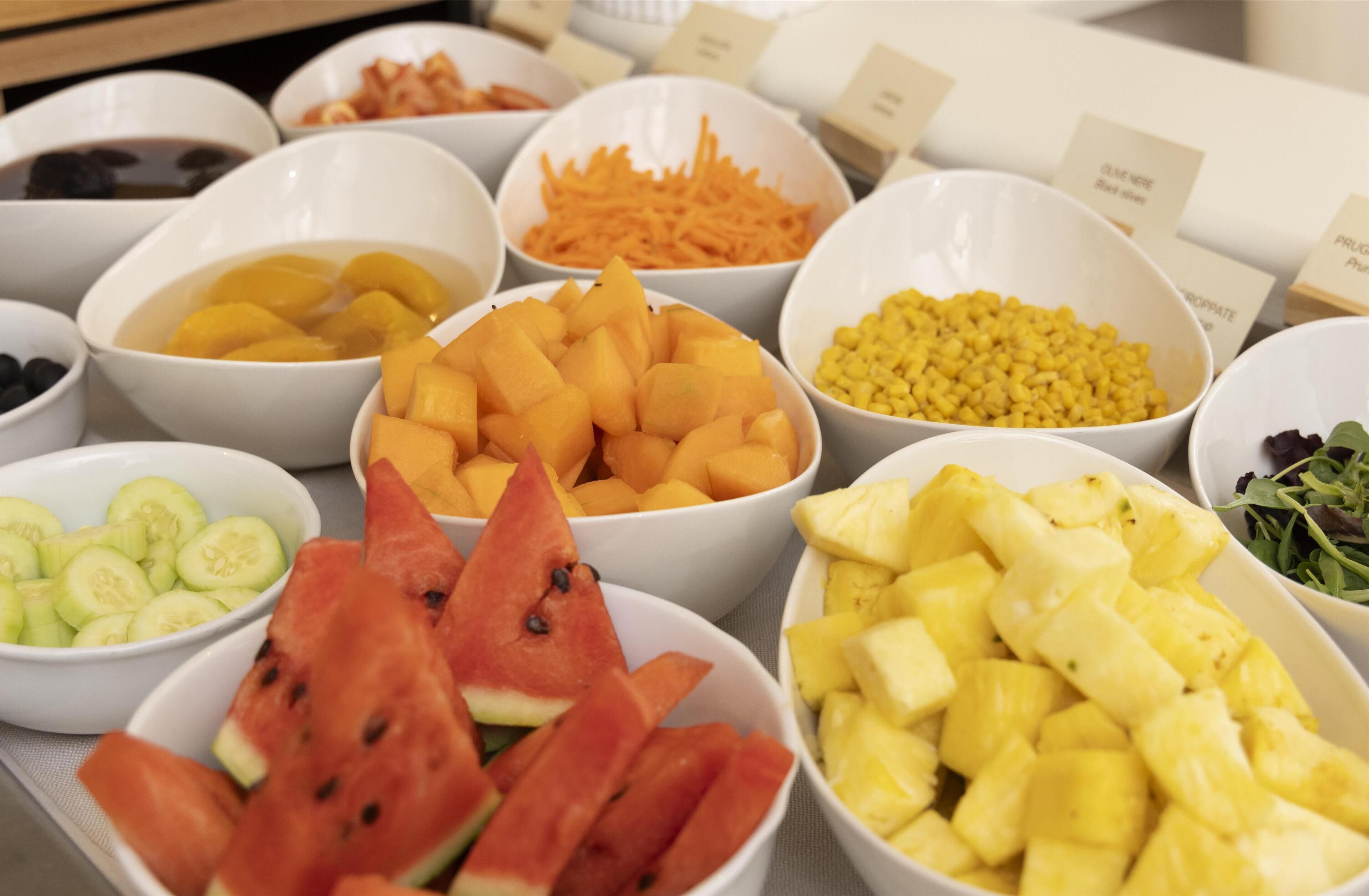 Diversas frutas e legumes dispostos em tigelas, com etiquetas identificando os tipos.