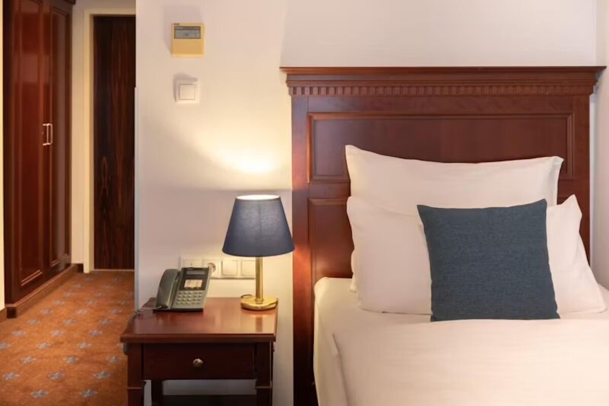 Quarto de hotel com uma cama, um abajur, um telefone e uma cabeceira de madeira.