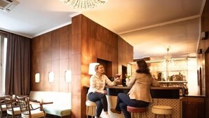 Uma área de bar com painéis de madeira, balcão, banquetas e um espaço de estar com cadeiras.
