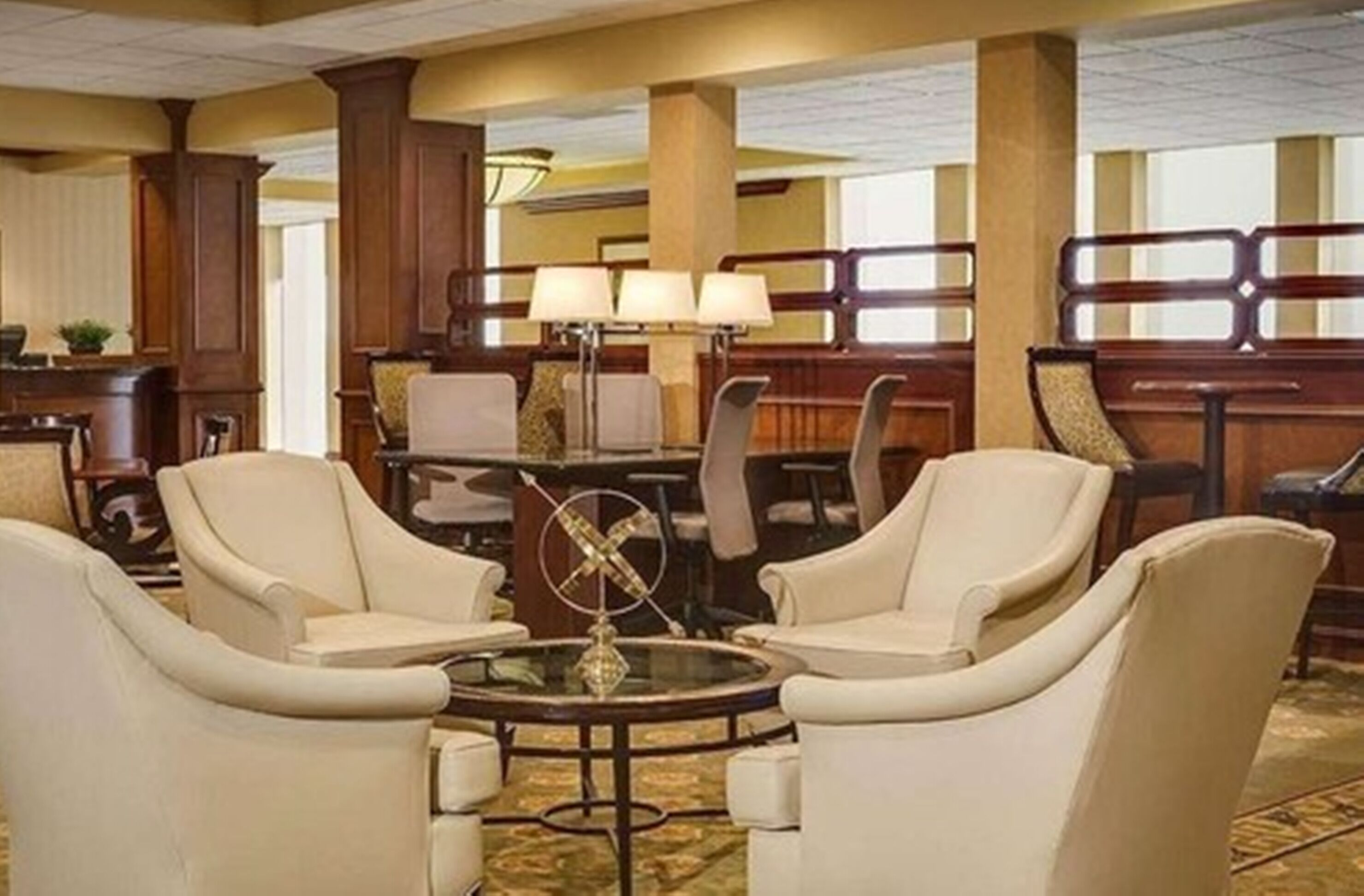 Um hall de hotel com uma mesa redonda, várias poltronas e um balcão de recepção.