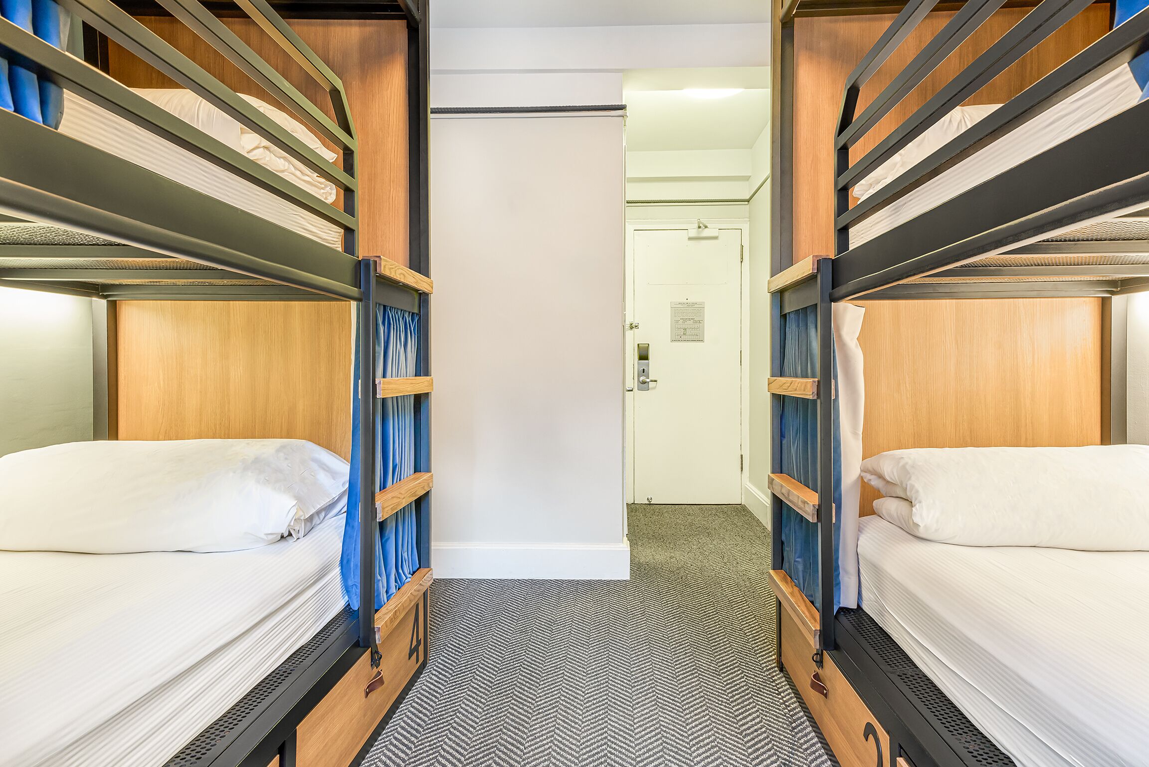 Quarto com beliches, uma porta e piso coberto por carpete.