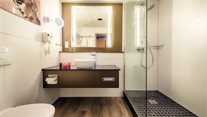 Um banheiro moderno com vaso sanitário branco, pia com espelho acima e box de vidro.