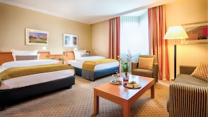 Quarto de hotel com duas camas, um sofá, uma mesa com frutas e uma luminária.