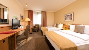 Quarto de hotel com escrivaninha, televisão, duas camas, uma cadeira e um abajur.