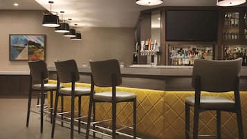 Uma área de bar com quatro banquetas, um balcão com diversos tipos de bebidas e uma televisão instalada acima do bar.