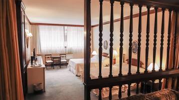 Quarto de hotel com cama, escrivaninha, cadeira e janela com cortinas.