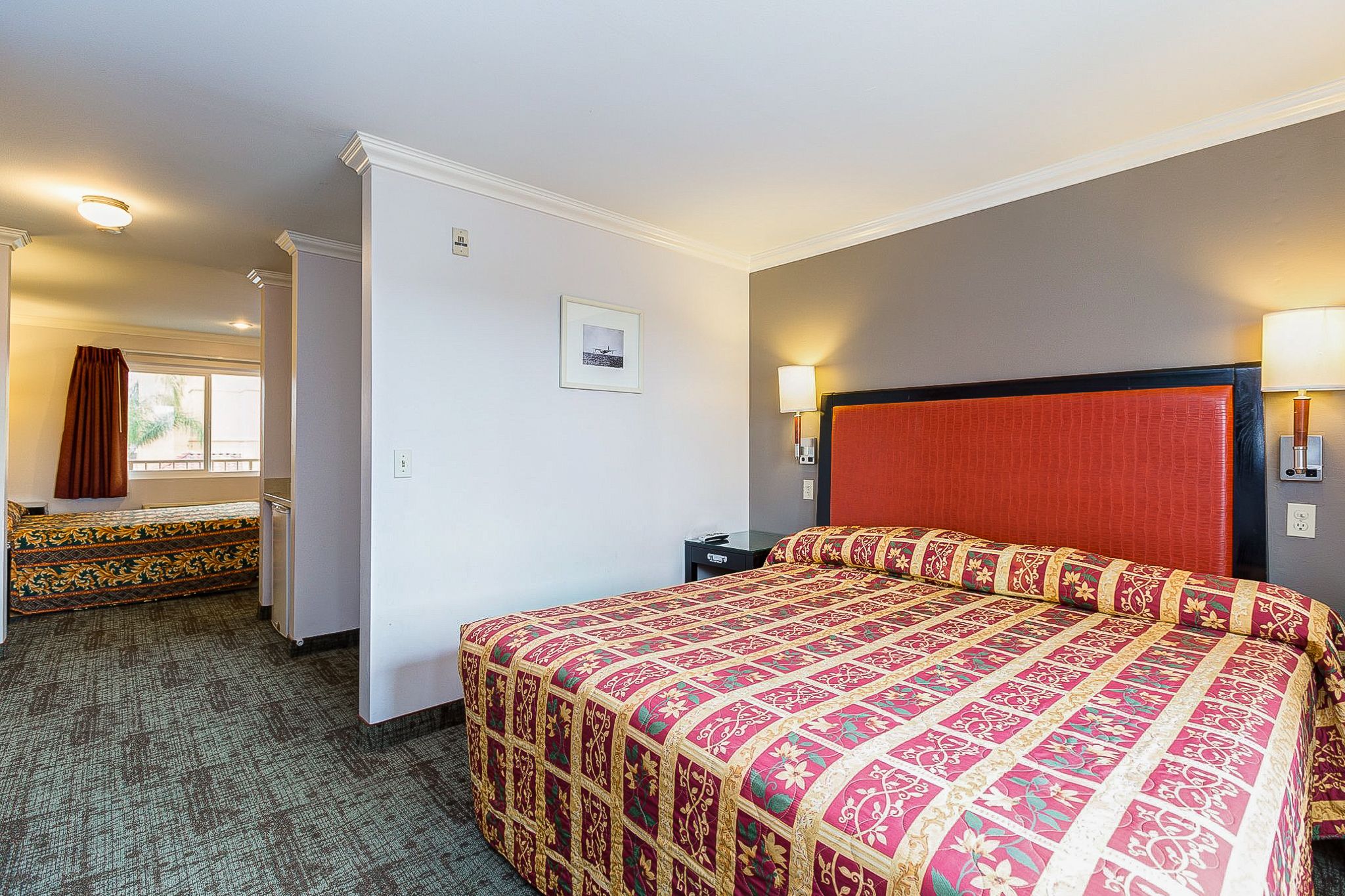 Quarto de hotel com uma cama grande, mesa de cabeceira, cortinas e um quadro na parede.