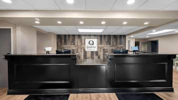 Uma área de recepção de hotel com dois balcões, uma placa com a inscrição 'Quality by Choice Hotels' e um letreiro na parede com a palavra 'BEM-VINDOS!'.