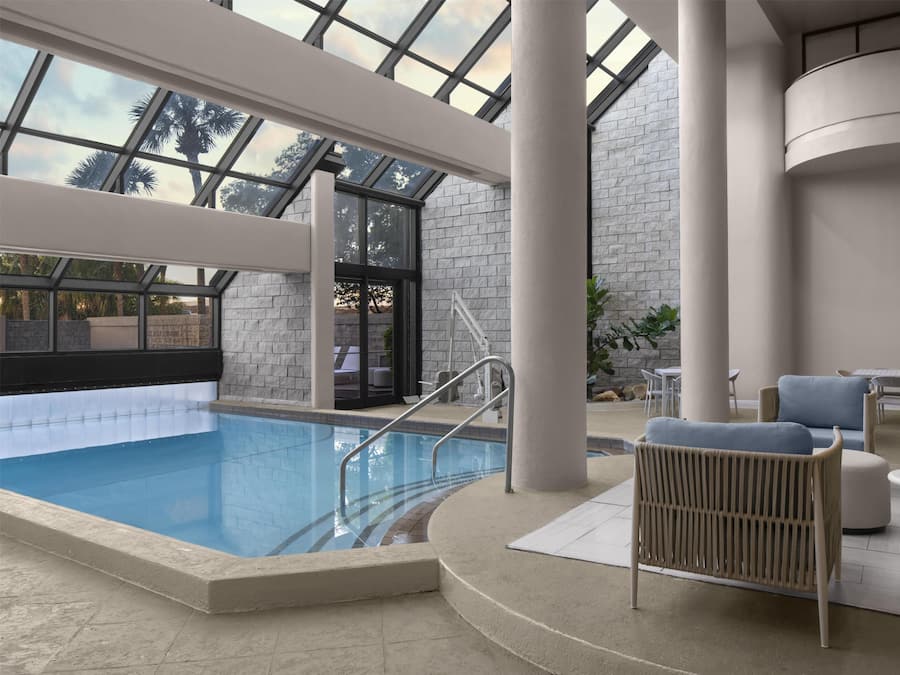 Piscina interior com teto de vidro, área de estar com assentos e parede de pedra.