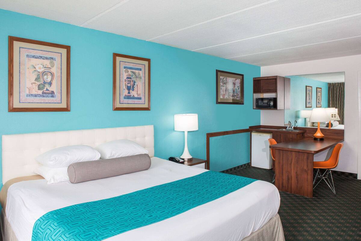 Quarto de hotel com cama, escrivaninha e cozinha compacta.