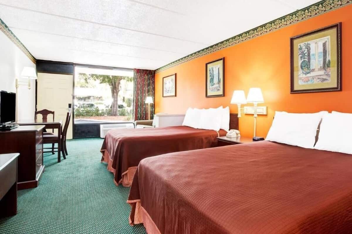 Quarto de hotel com duas camas, uma escrivaninha, uma cadeira, janela com vista e obras de arte nas paredes.