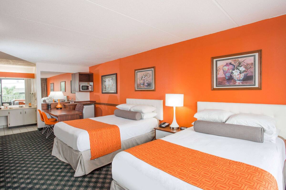 Quarto de hotel com duas camas, uma escrivaninha, uma cadeira e um micro-ondas.