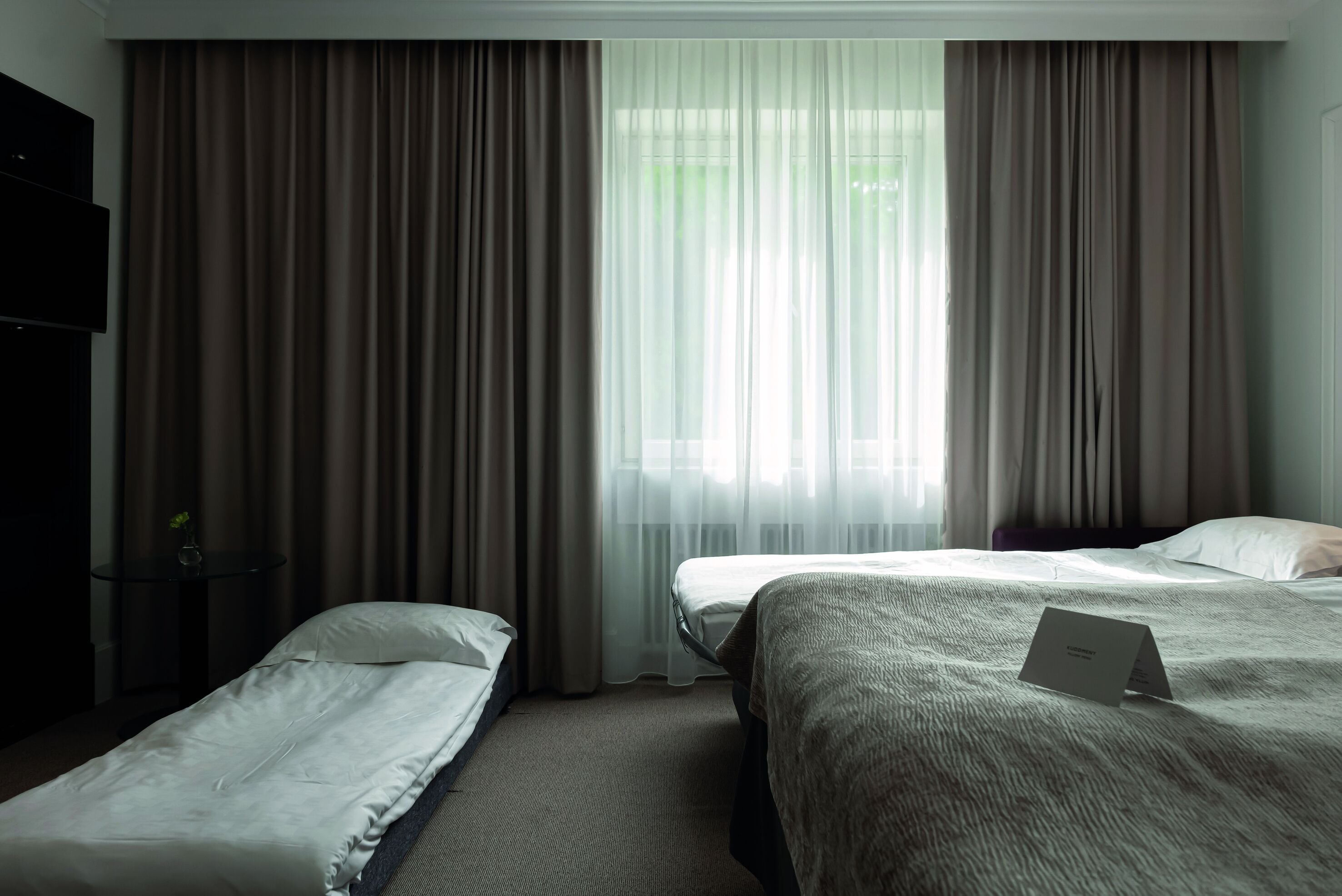 Quarto de hotel com duas camas, uma mesinha com um vaso e um laptop sobre uma das camas.
