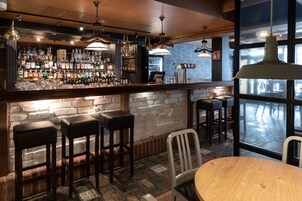 Uma área de bar com parede de tijolos, banquetas de madeira e luminárias pendentes.