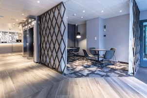 Um interior moderno com piso de madeira, uma área de refeições com cadeiras e uma mesa, e uma cozinha com bancada e cadeiras.