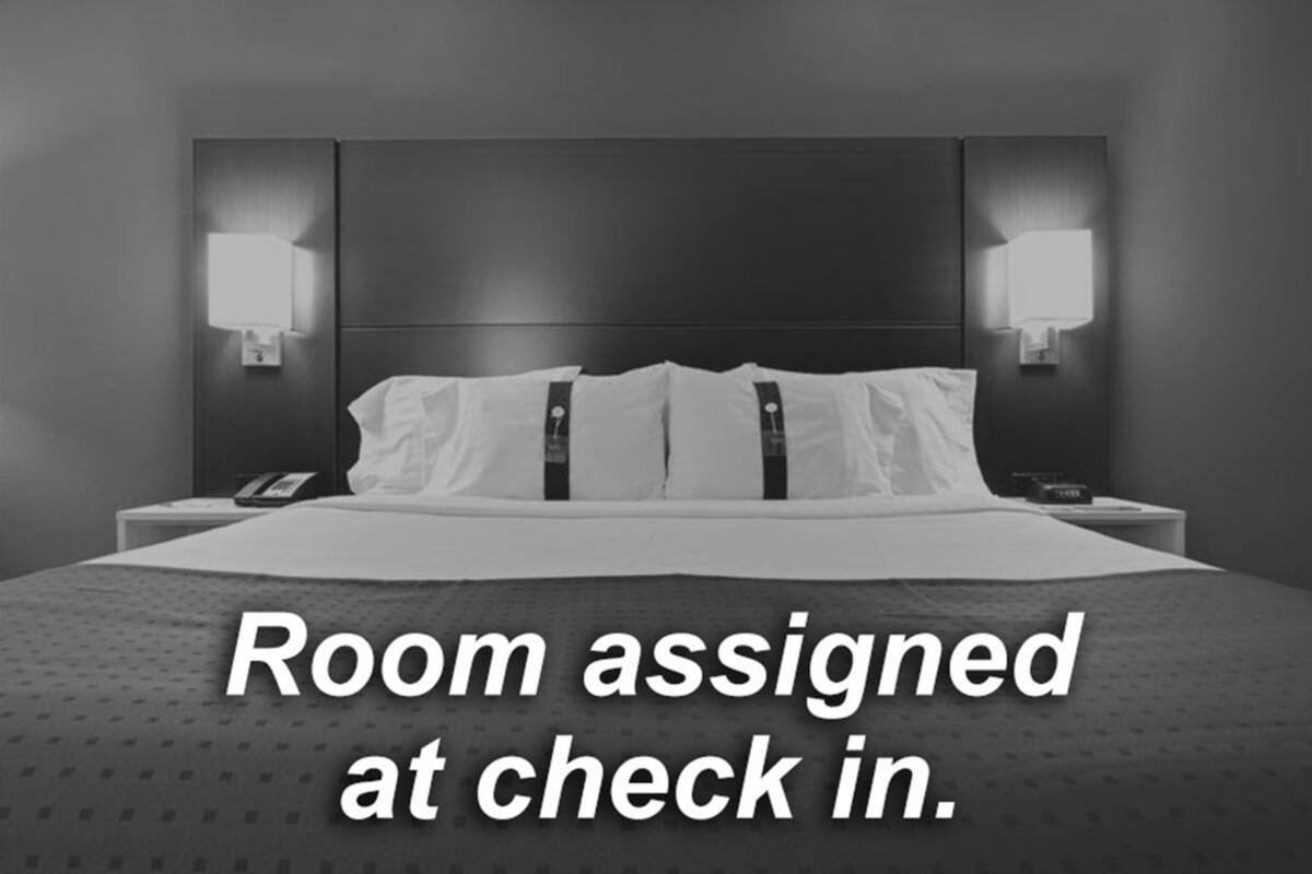 Quarto de hotel com uma cama grande, duas mesas de cabeceira e duas luminárias fixadas na parede.